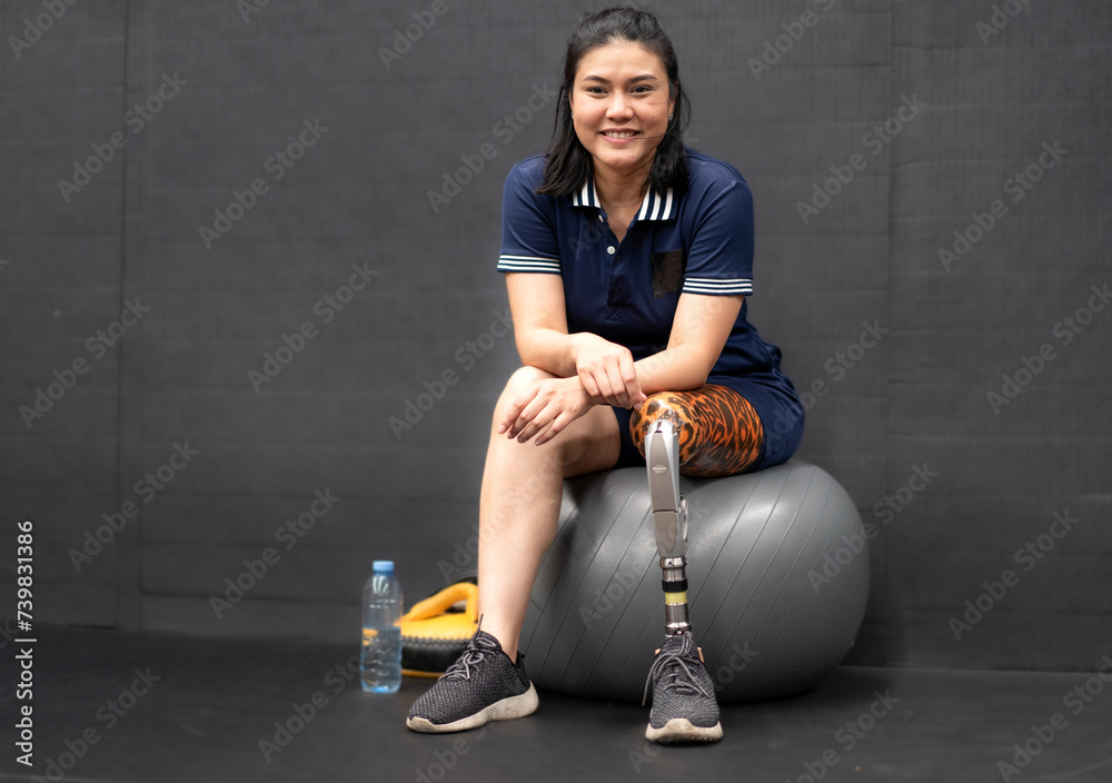 Woman with prosthetic leg sits relaxing on ball in gym. Asian female ...