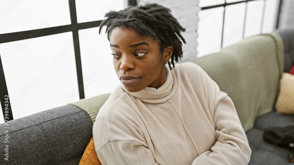 African american woman with dreadlocks sitting thoughtfully on a sofa ...