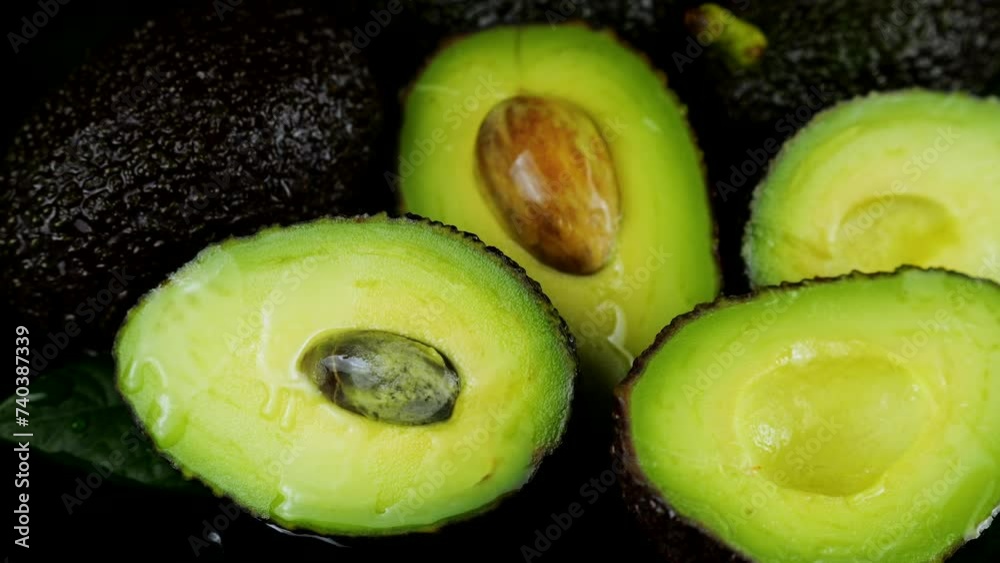 Drops of water fall on avocado fruits with leaves on a black background ...
