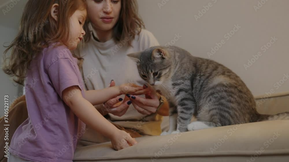 Mother and her little daughter feeding cat in living room. Happy family ...