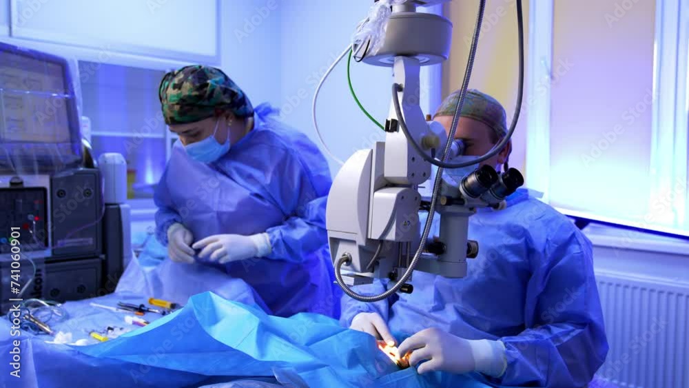 Mid-aged mal surgeon sitting behind the microscope performs ophthalmic ...