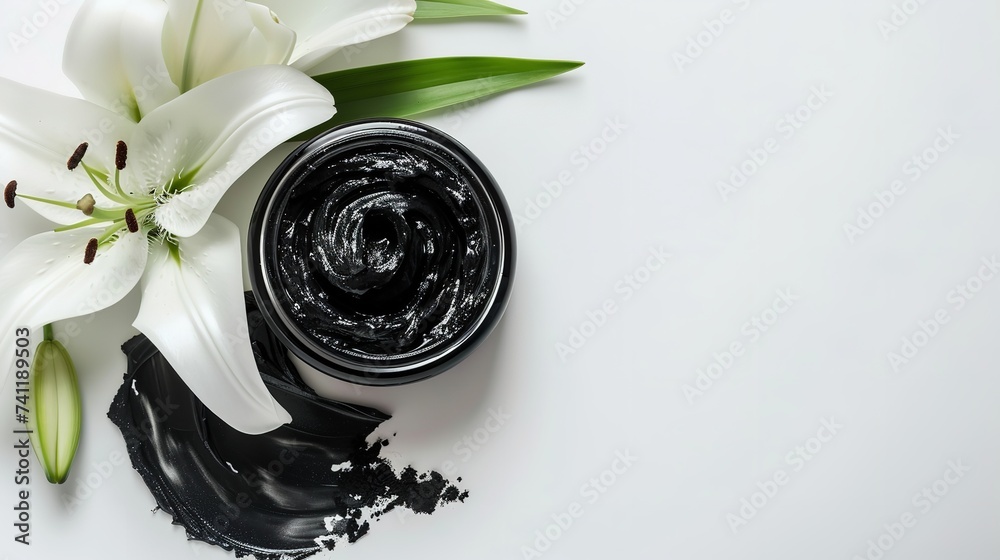White lily bloom over white setting with black activated charcoal paste ...