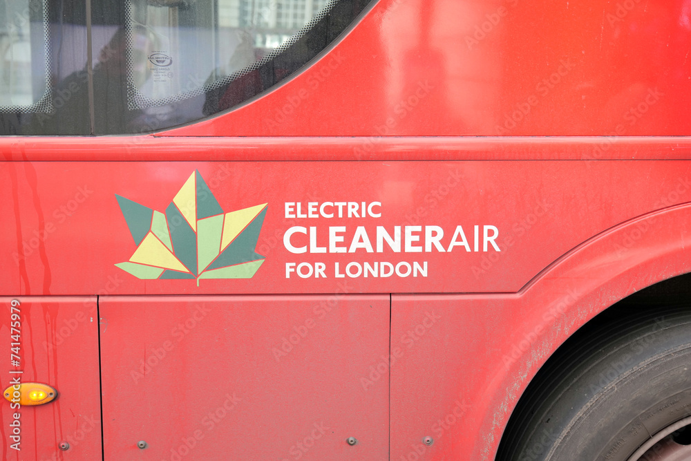 The side of a red electric London bus has a leaf emblem and wording to ...