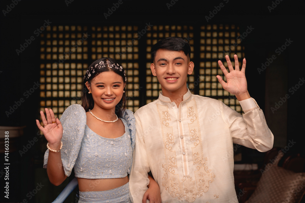 A young friendly couple in Filipino traditional clothing waving hi ...