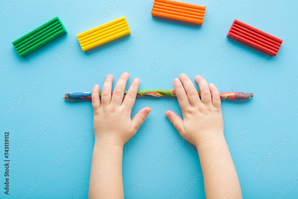 Baby boy hands rolling colorful stick from modeling clay on light blue ...