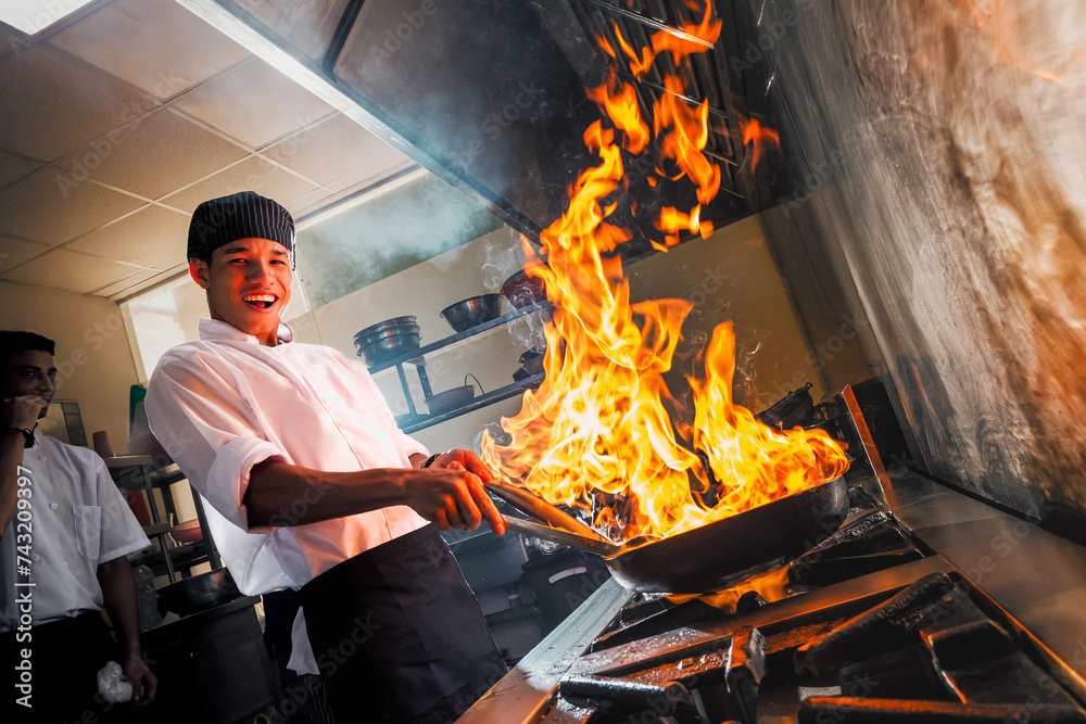 Young chef in the restaurant kitchen making flambe in the frying pan ...