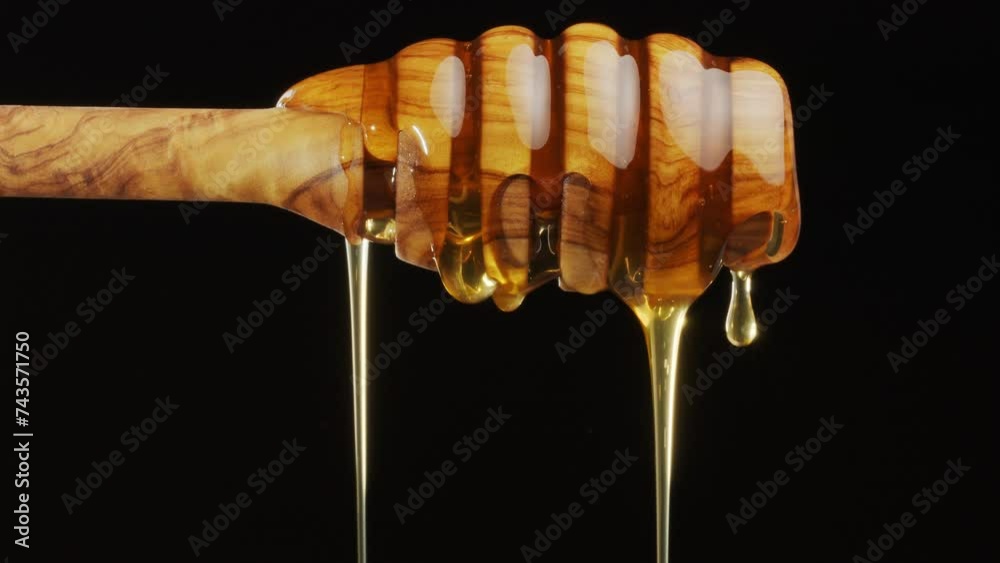 Drops of honey flow from a wooden honey dipper and slowly drip down ...