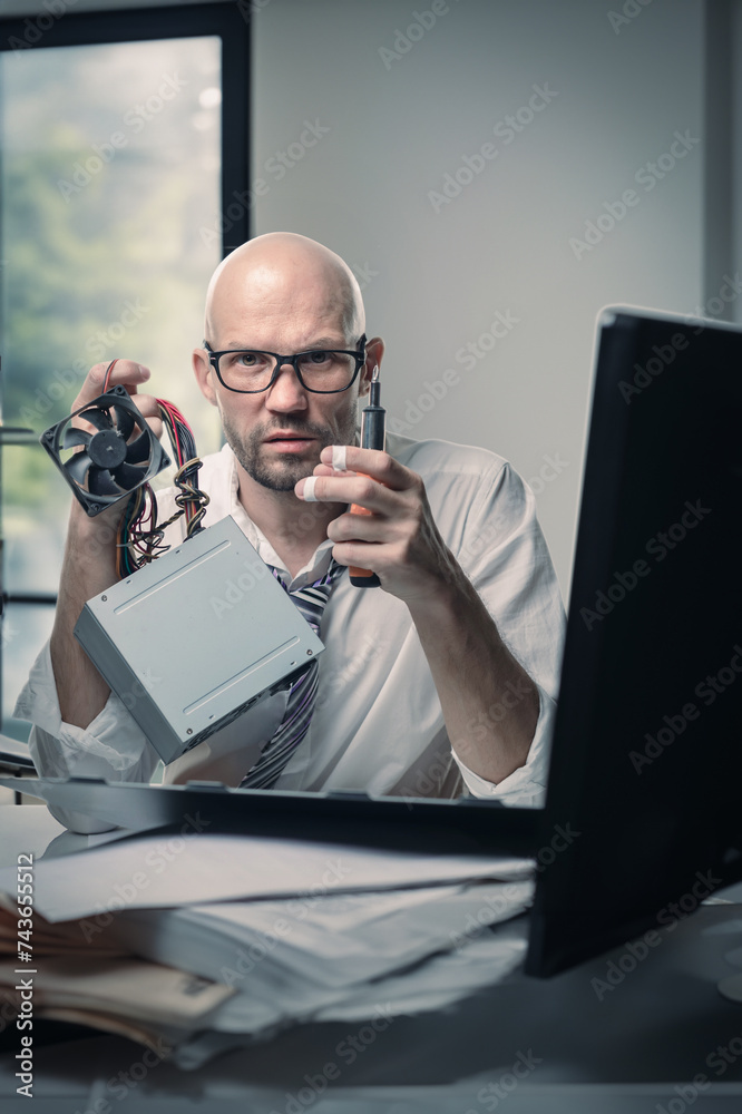 a young bald male office worker sitting at his workplace next to a ...