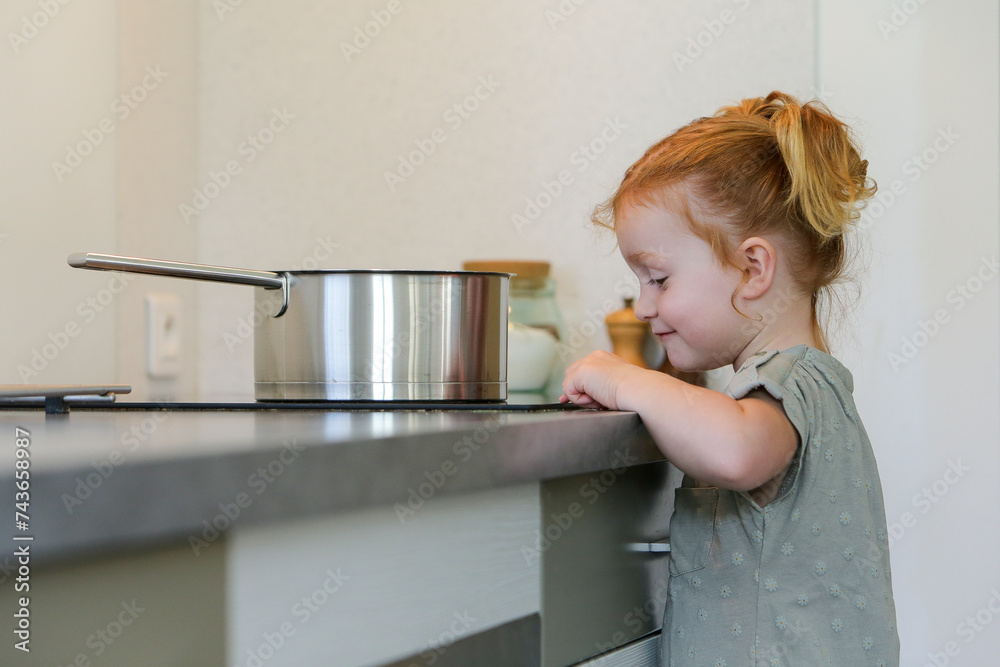 Little girl in a kitchen with a metal pan touching the hob knobs Stock ...
