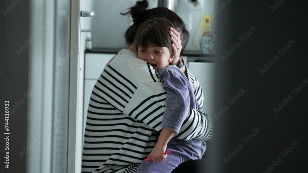 Tender mother consoles son in loving embrace in candid kitchen scene ...