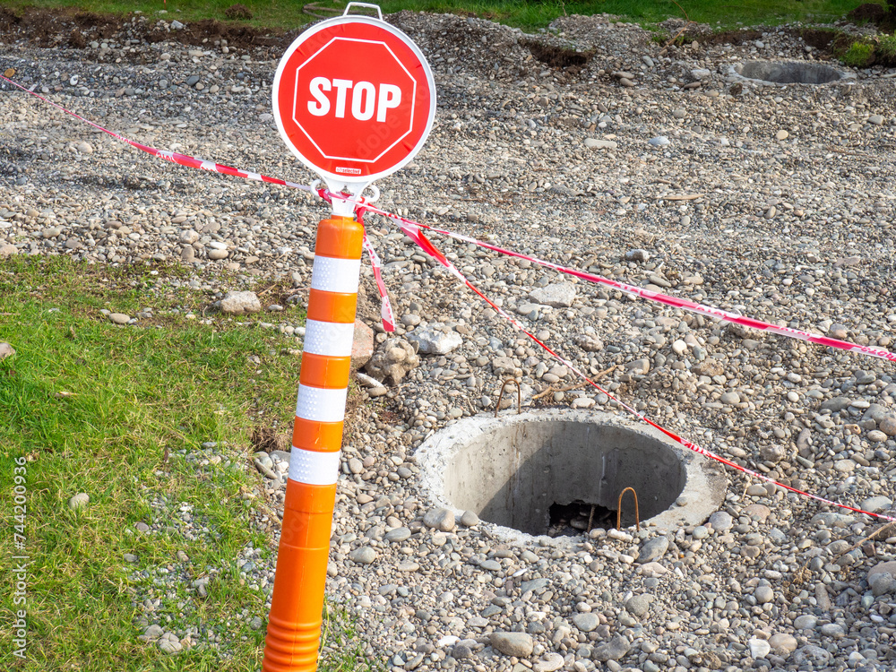 A stop sign in a park in front of an open manhole. Danger lies ahead. A ...