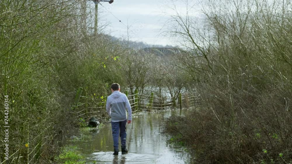 Young farmers boy walking along a flooded country path and wading ...