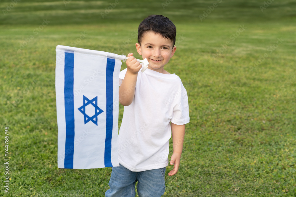 Smiling young boy proudly displaying the flag of Israel in a sunny park ...