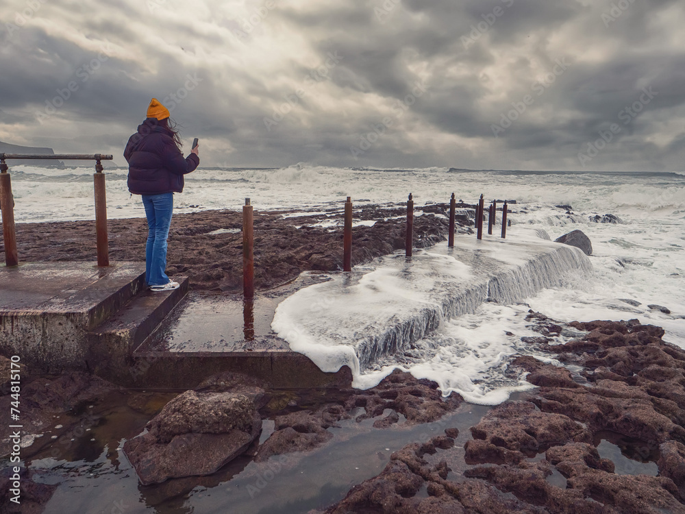 Foto de Teenager girl filming ocean on her smart phone. Dark dramatic ...