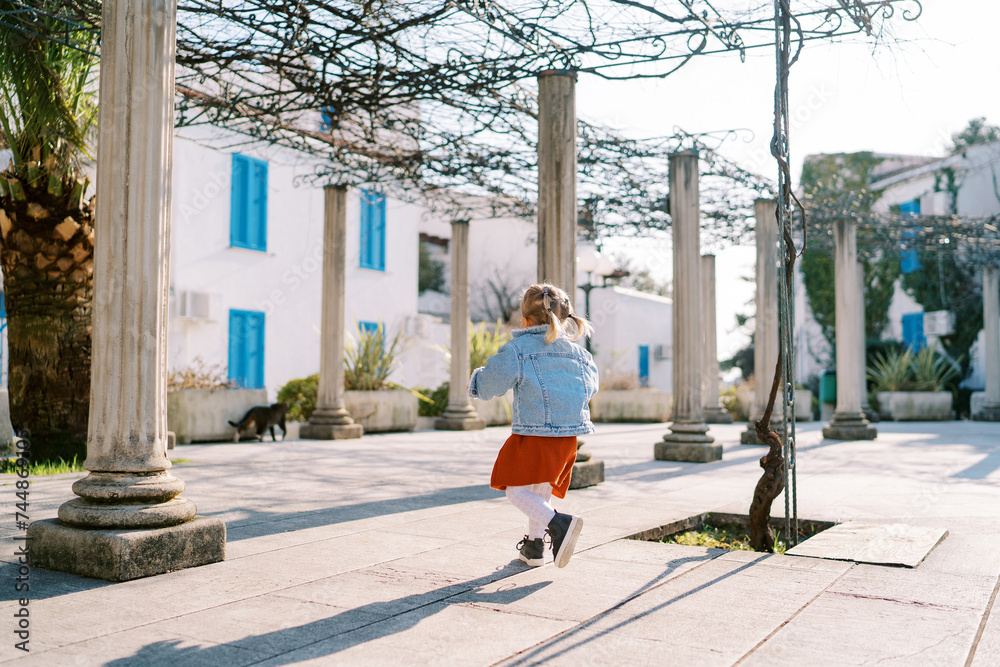 Little girl walks between pergola columns in a garden near a three ...