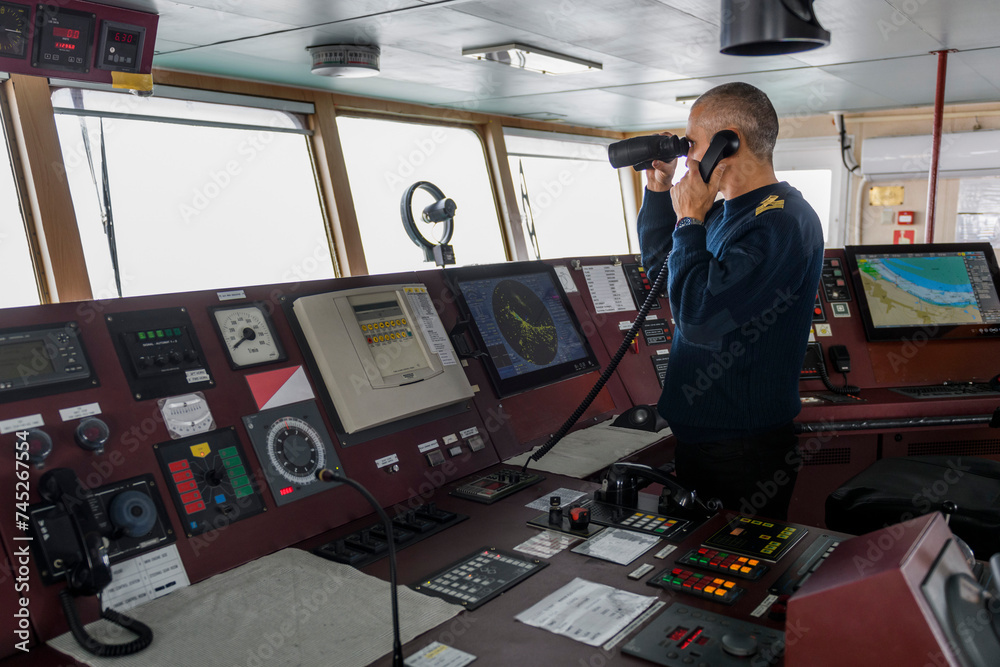 Officer on watch with radio and binoculars on the navigational bridge ...