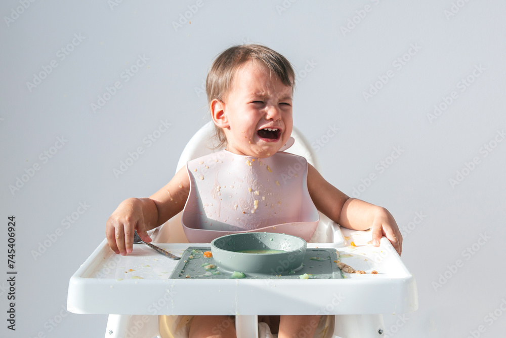 cute crying baby sitting eating lunch in high chair at home on white ...