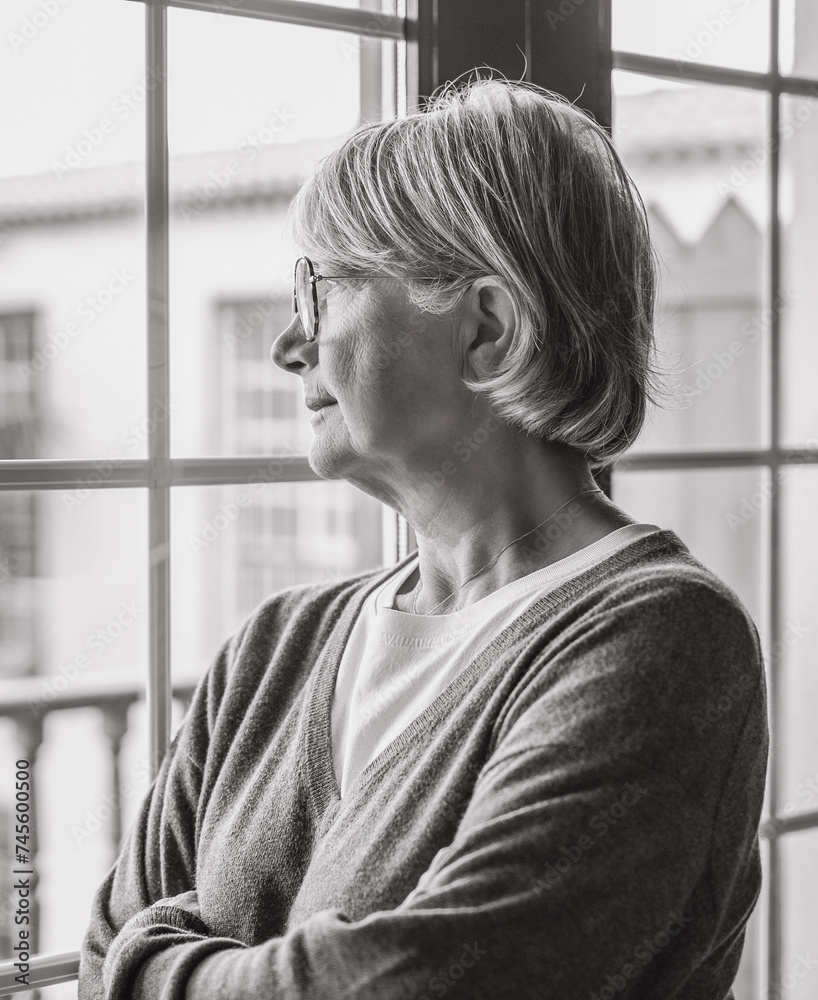 Black and white portrait of senior woman standing at window looking ...