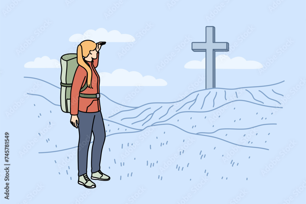 Woman pilgrim stands near large christian cross on hills during hike to ...