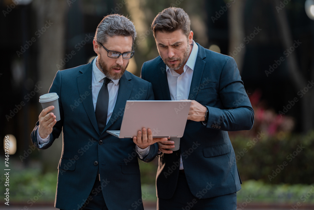 Two handsome young businessmen in classic suits using laptop. Freelance ...