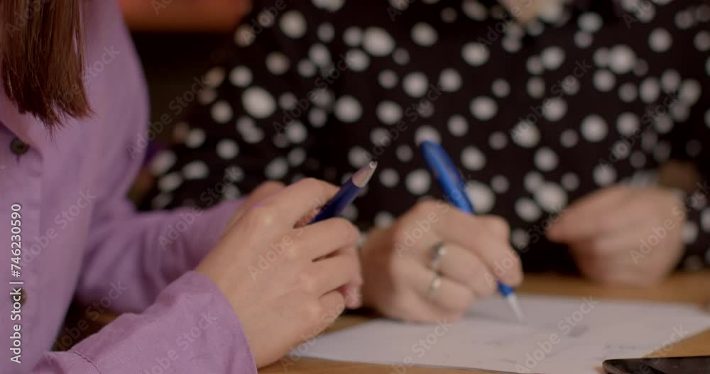 Close-up teacher explains task to student, draws with pen on paper ...