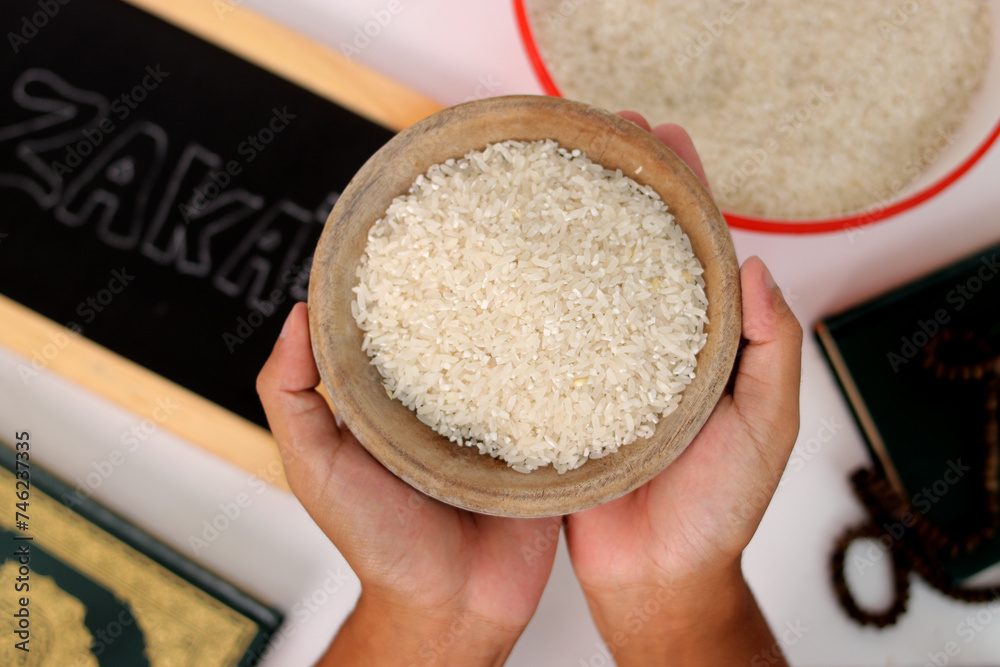 Hand holding a bowl of rice for Zakat al-Fitr, with the Holy Quran and ...