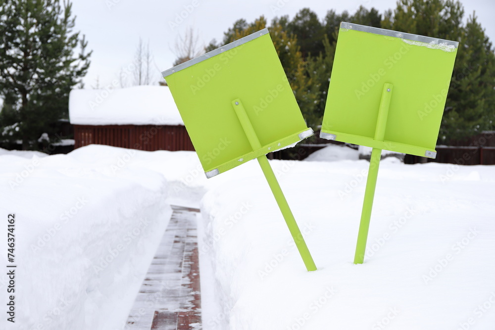 A two green wooden shovels for snow stand in a snowdrift near pathway ...