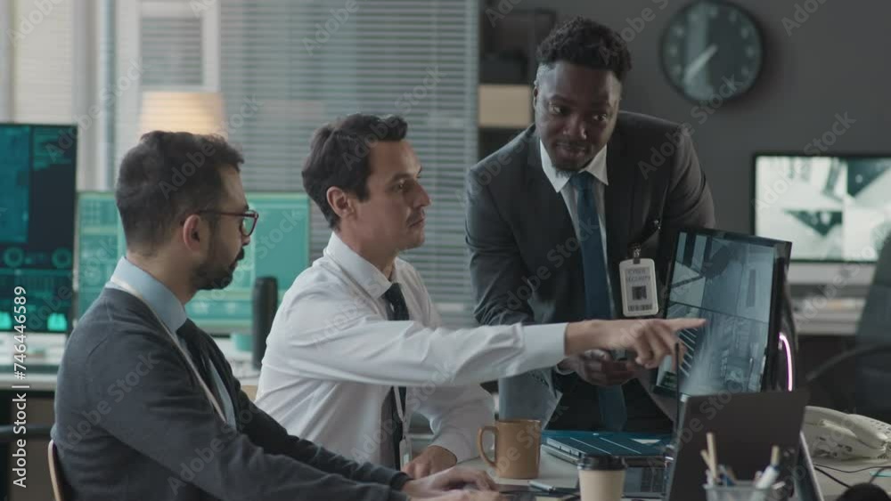 Medium shot of three multiracial male cybersecurity workers looking at ...