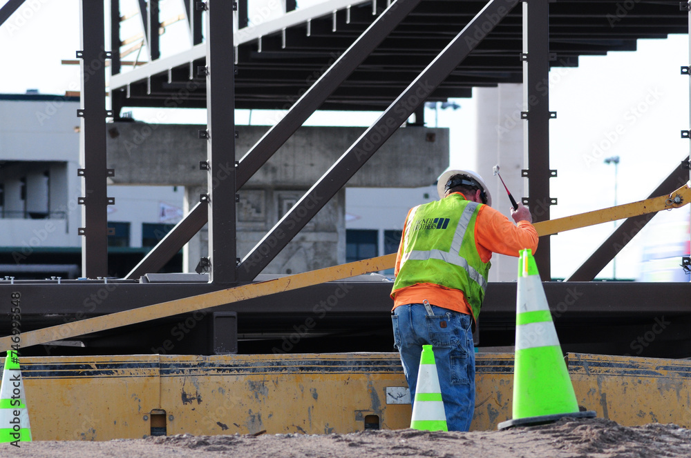 A construction worker wearing a hard hat and safety vest uses a hammer ...