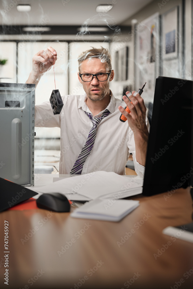 Frustrated sad young man repairing computer hardware in modern office ...