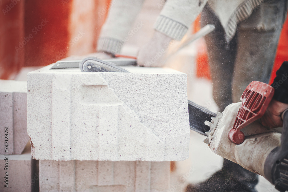 Workers cutting autoclaved aerated concrete block with chainsaw closeup ...