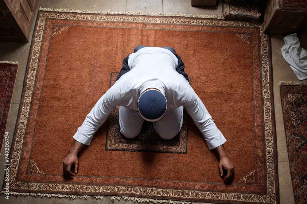 A muslim man with cap kneeling on a prayer mat facing Mecca in a small ...