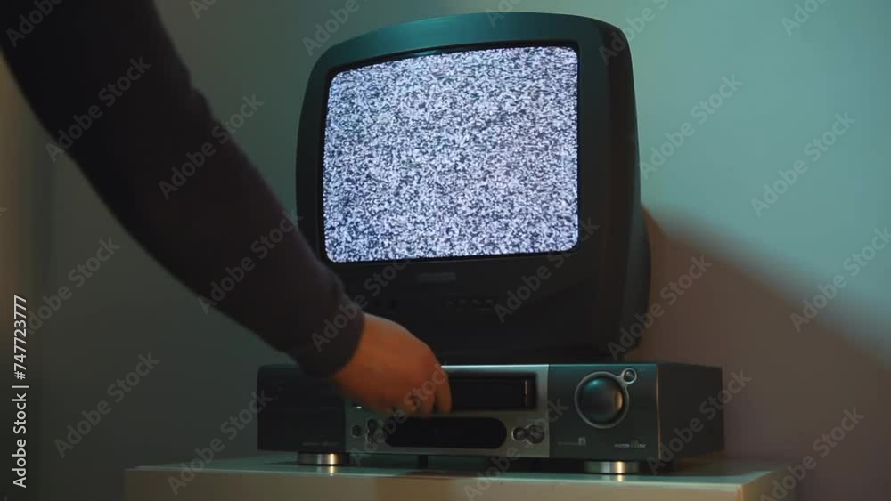 Close-up of a man with his hand inserting VHS for viewing on an old TV ...