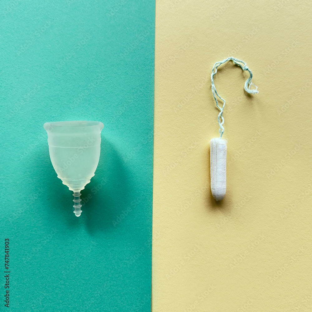 A reusable silicone menstrual cup and standard tampon on a green and ...
