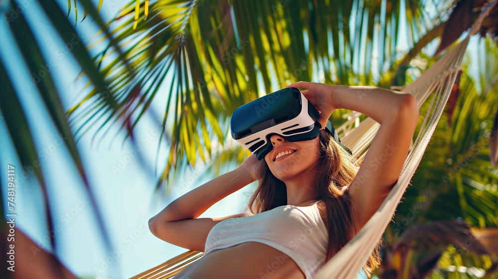 Young woman relaxing in a hammock using a VR headset on tropical beach. Modern innovative ...