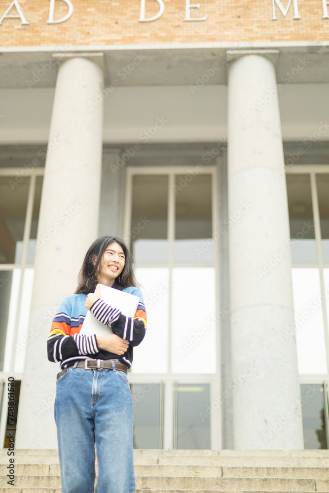 young Chinese male student happy at the door of a building with columns ...