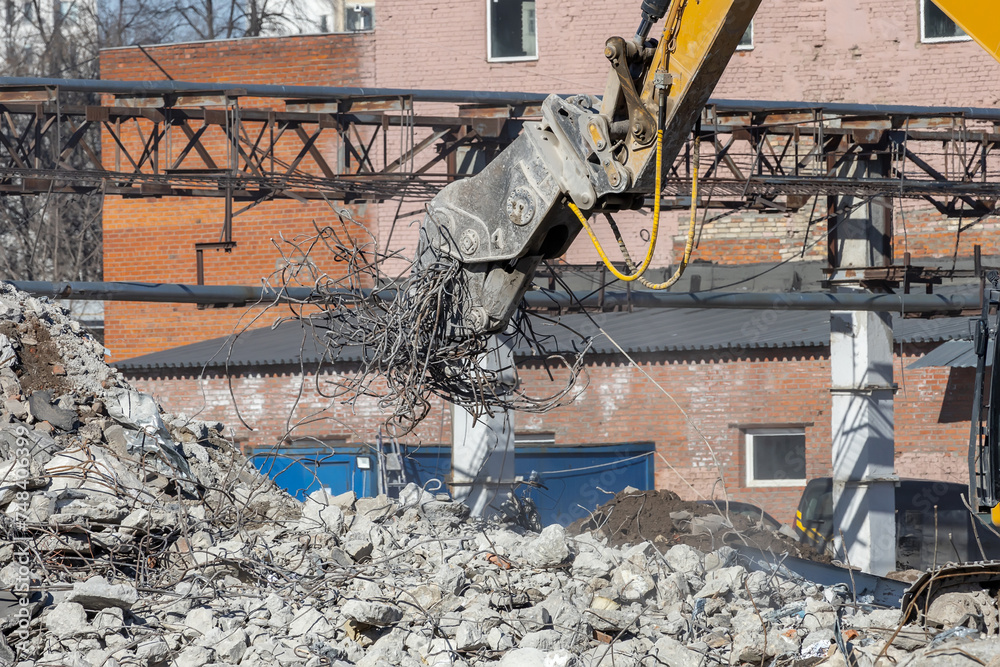 A yellow excavator with a hydraulic concrete pulverizer lifts a pile of ...