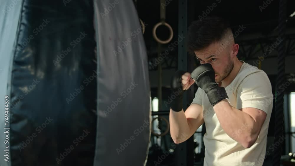 Strong man in boxing gloves training with punching bag in gym ...
