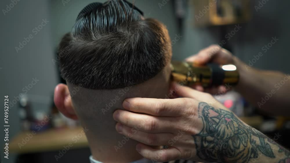 A barber man with a tattoo on his arm makes a haircut to a brunette guy ...