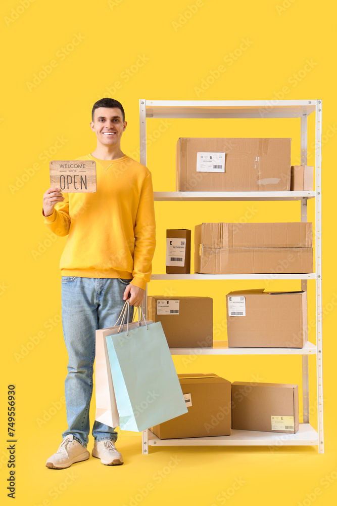 Male online store seller with OPEN sign, shopping bags and parcel boxes ...