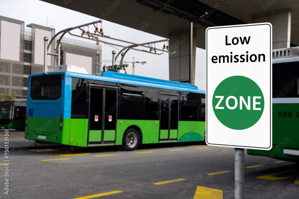 Road sign "Low emission ZONE" on a background of green electric buses ...