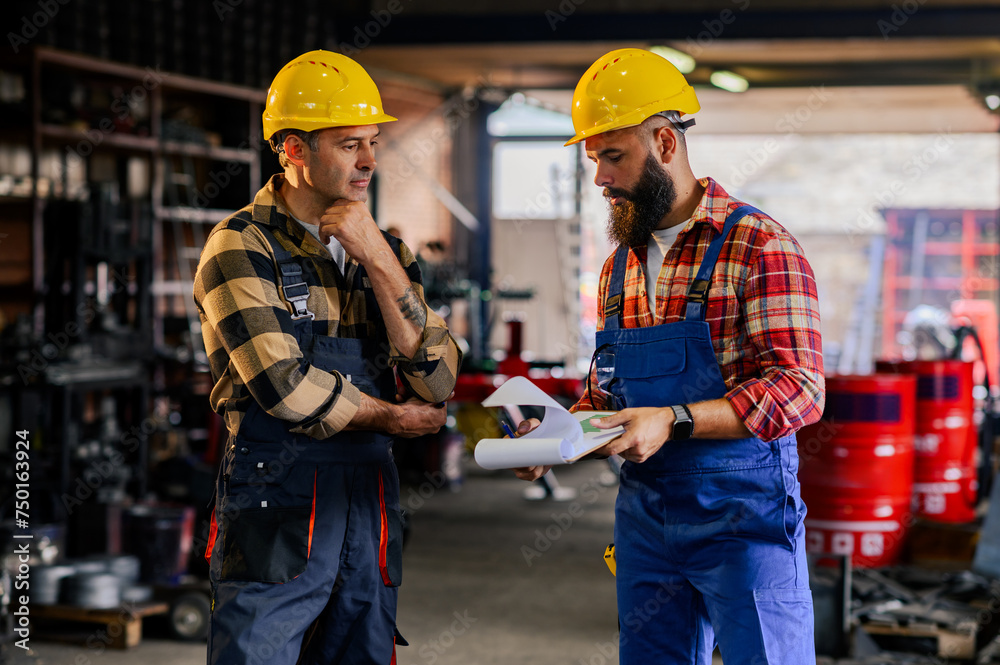 Caucasian mechanic reading his notes while his colleague is listening ...