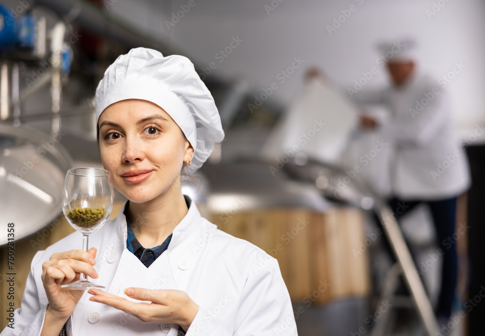 Confident successful female brewmaster in white uniform showing hop ...