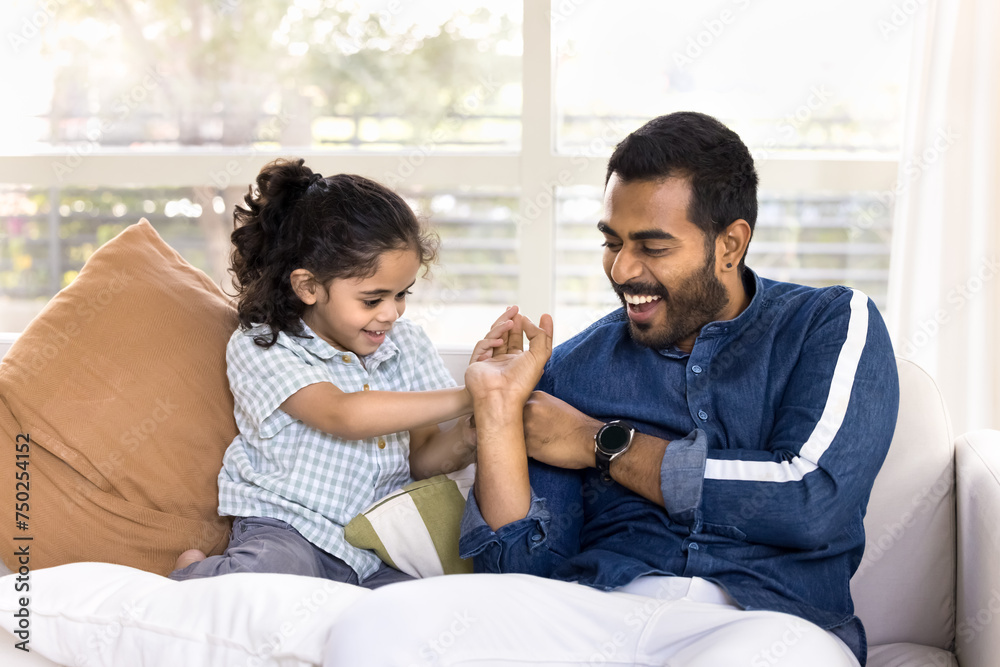 Positive young Indian dad playing fight with active little daughter kid ...