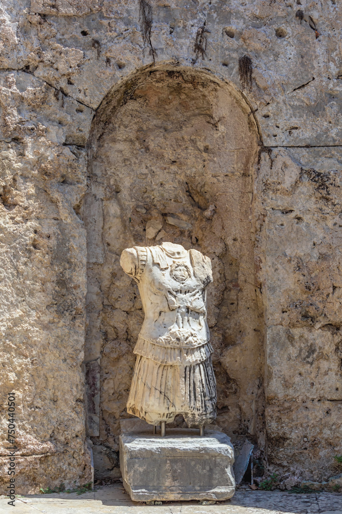 Headless ancient stone statue in Roman armour stands before a weathered ...