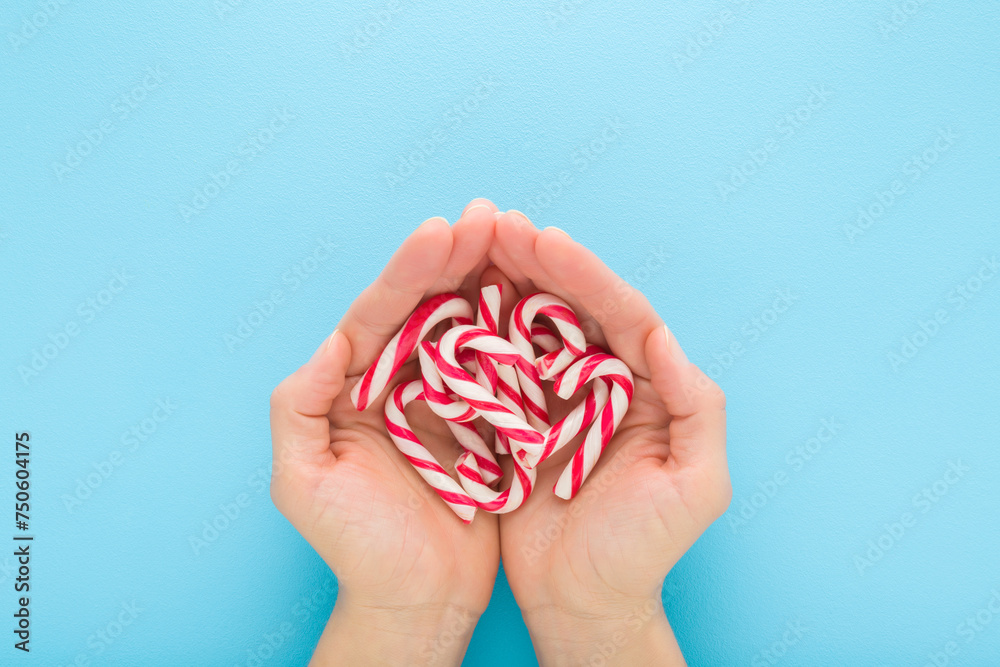 Red white candy canes in young adult woman opened palms on light blue ...