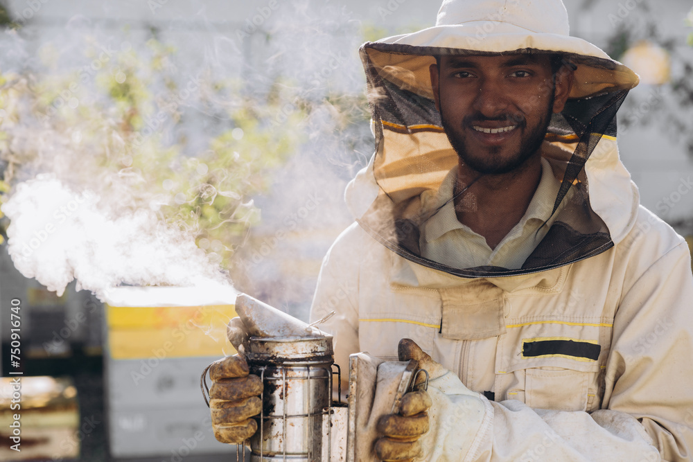 Happy smiling Indian male Beekeeper smoking honey bees with bee smoker ...