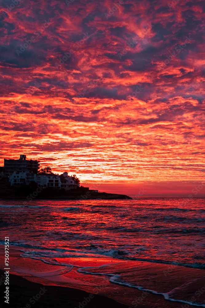 Red sunset at the beach with town in silhouette and dramatic sky with ...