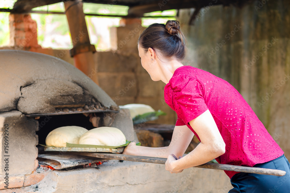 Woman placing bread dough to bake in a rustic wood-fired oven. The ...