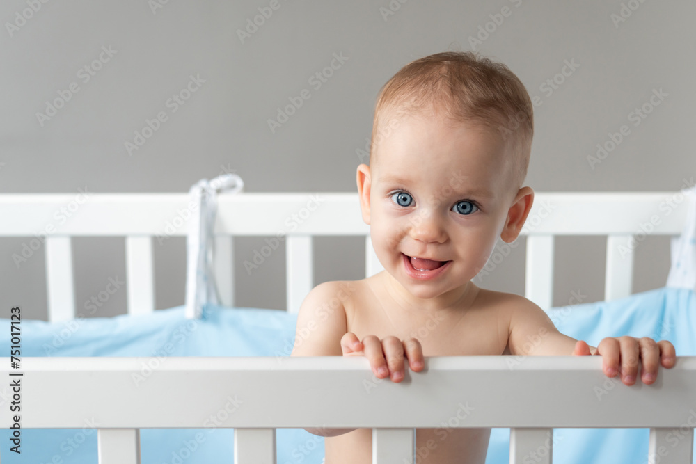 The baby looks with a trusting and kind look while standing in a crib ...